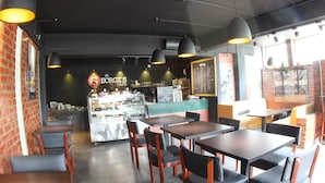 Interior de café com paredes de tijolo, mesas e cadeiras de madeira, iluminação pendente e um quadro de cardápio à vista.