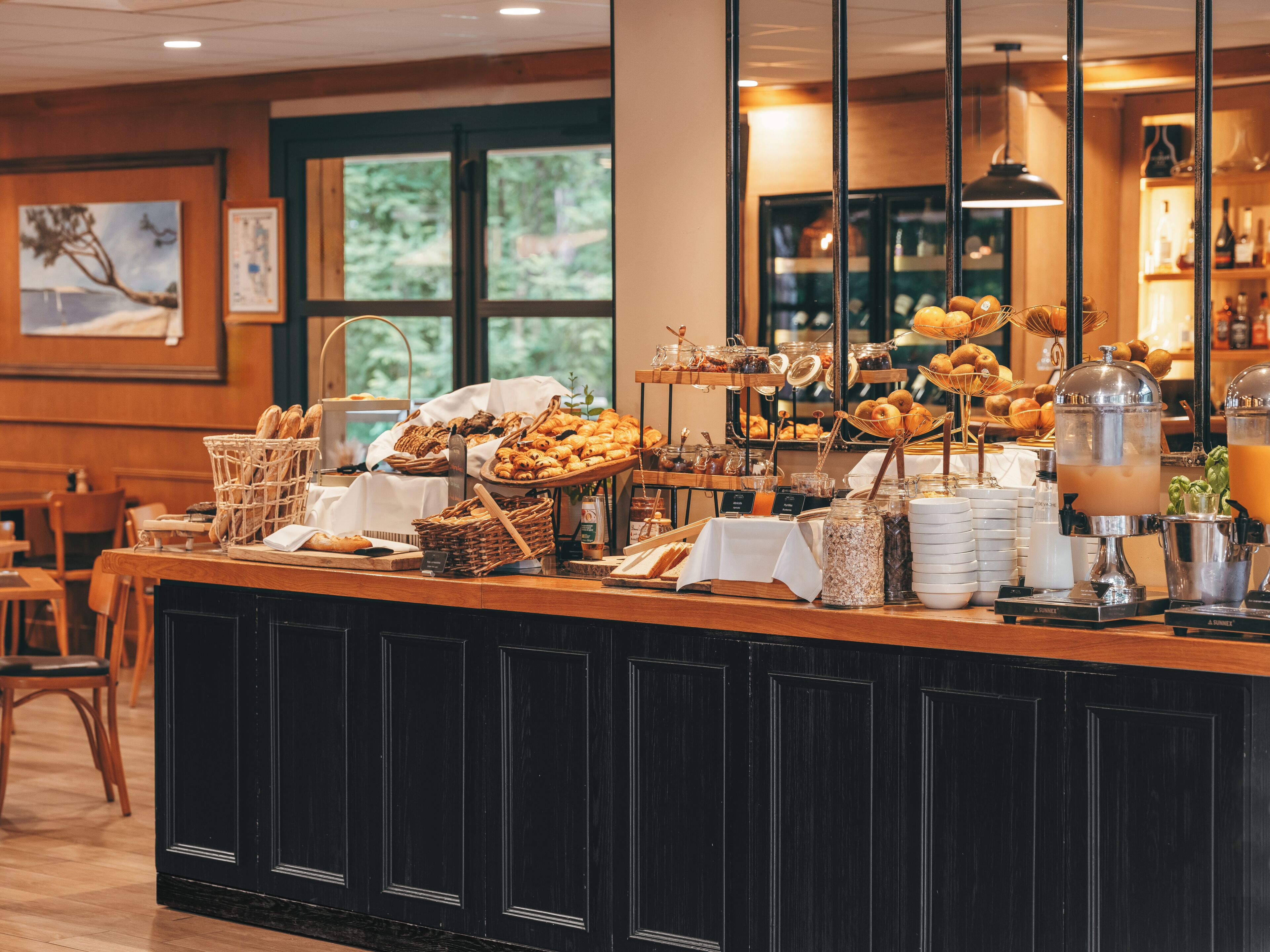 Balcão de buffet com diversos alimentos, uma máquina de café e uma área de estar com cadeiras.