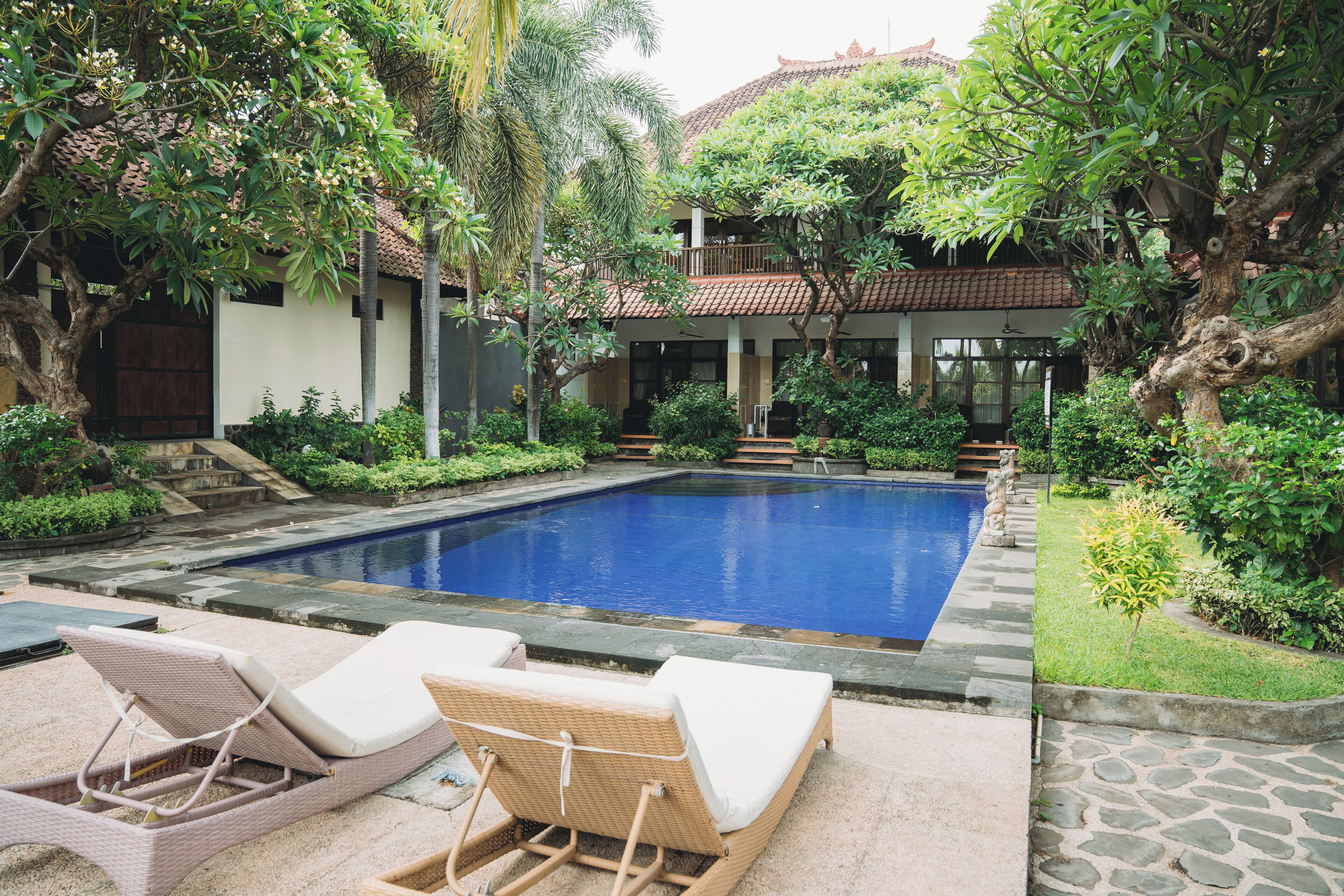 Área de piscina com espreguiçadeiras, caminho de pedra e vegetação exuberante.
