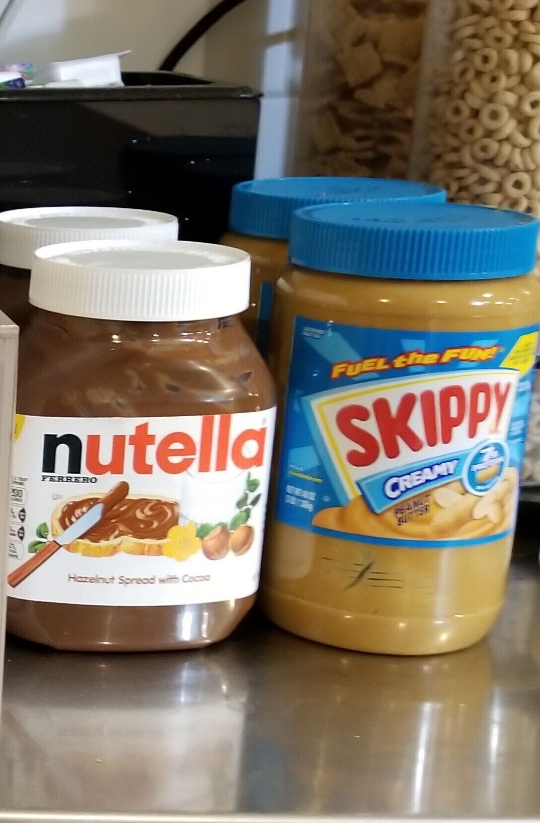 Dois potes de Nutella e um pote de pasta de amendoim cremosa Skippy em uma bancada de cozinha.