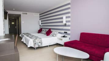 Quarto de hotel com cama, escrivaninha, sofá vermelho e uma pequena mesa.