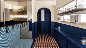 Um hall de hotel moderno com piso xadrez, esquema de cores azul e branco, área de estar com estofados estampados e prateleiras exibindo comodidades.