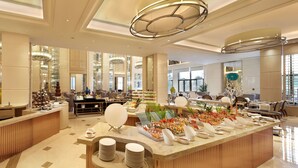 Um amplo hall de hotel com área de buffet, grandes espelhos e um lustre moderno.
