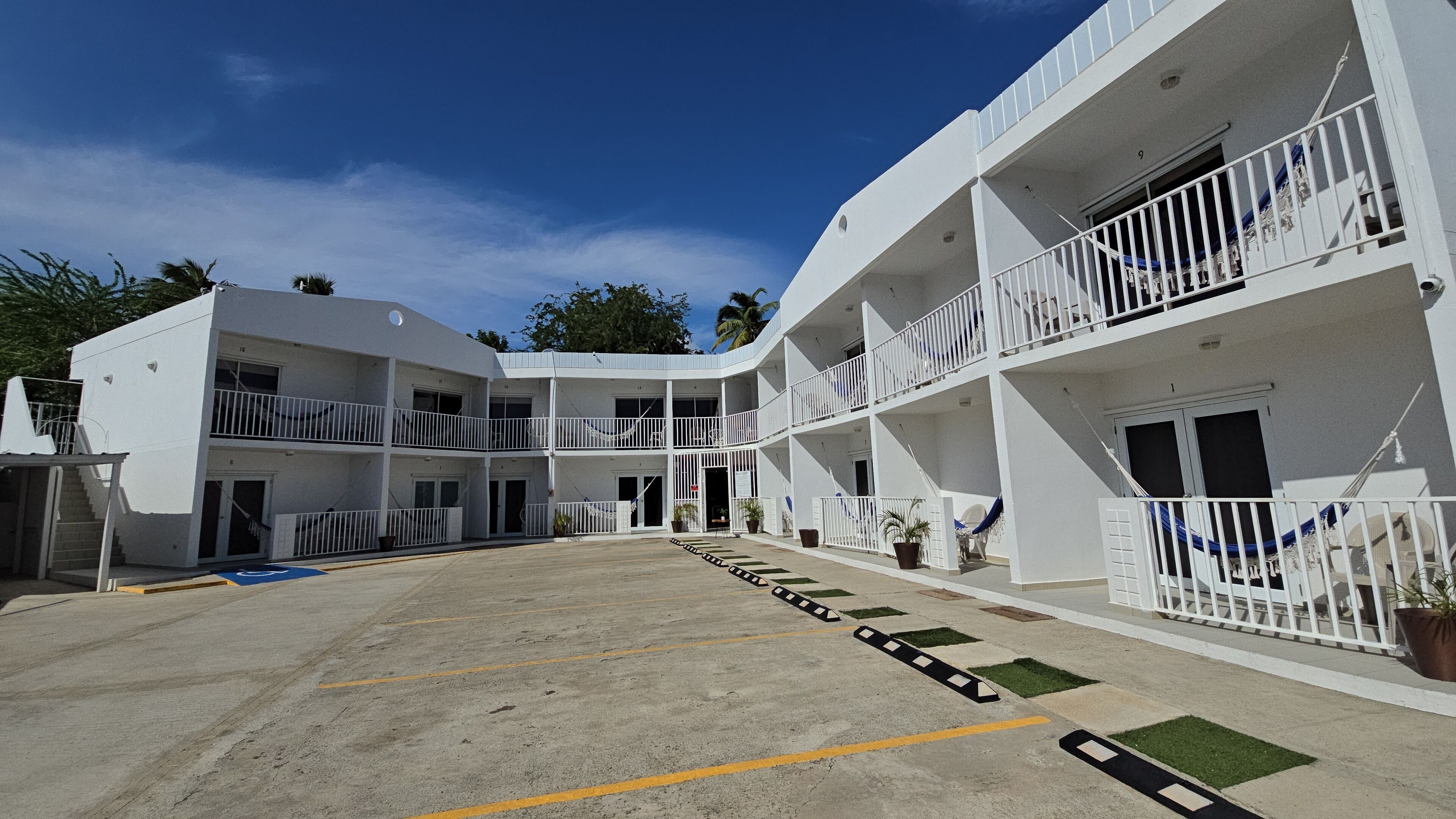 Um edifício com vários andares, varandas, área de estacionamento e plantas em vasos.