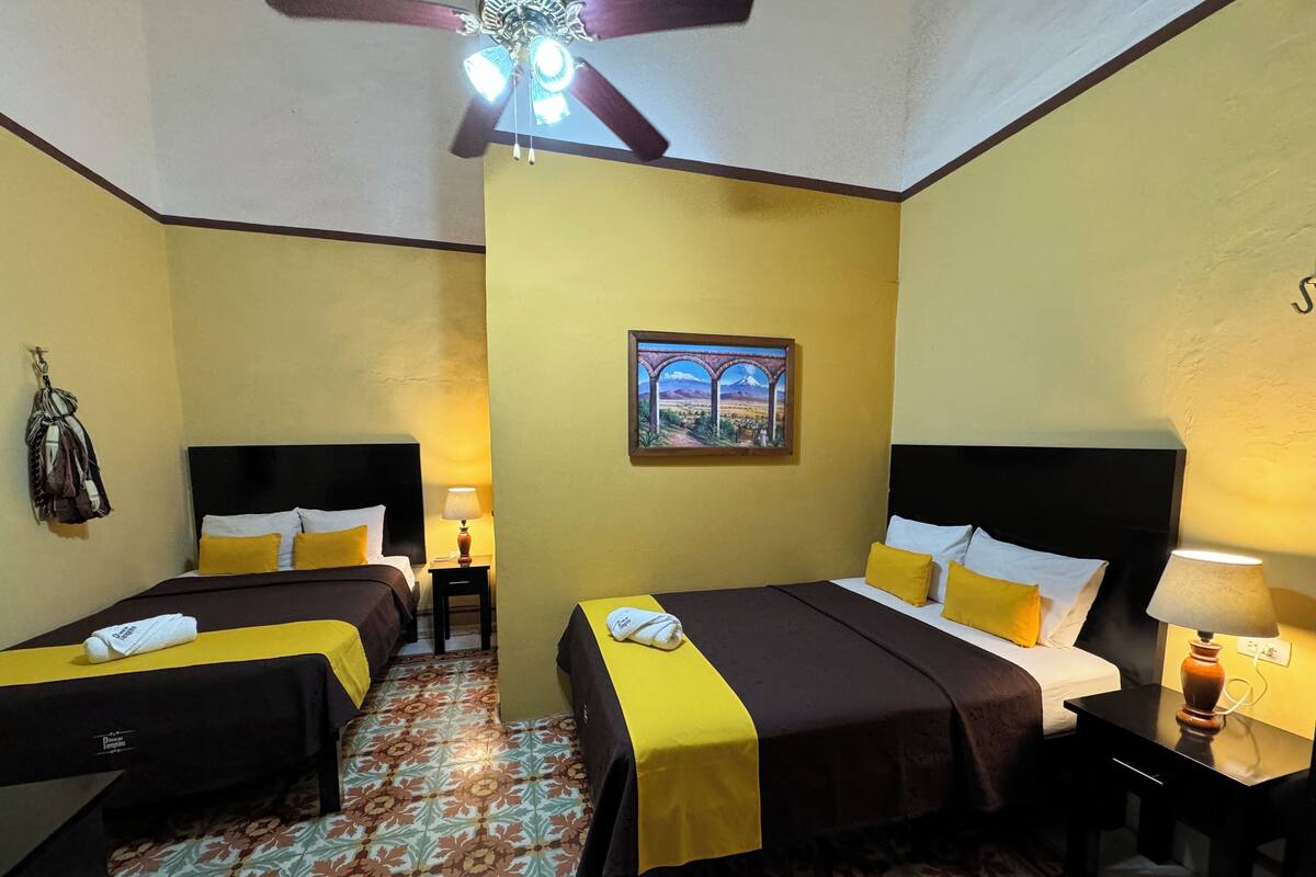Quarto de hotel com duas camas, um ventilador de teto, um quadro e um piso estampado.