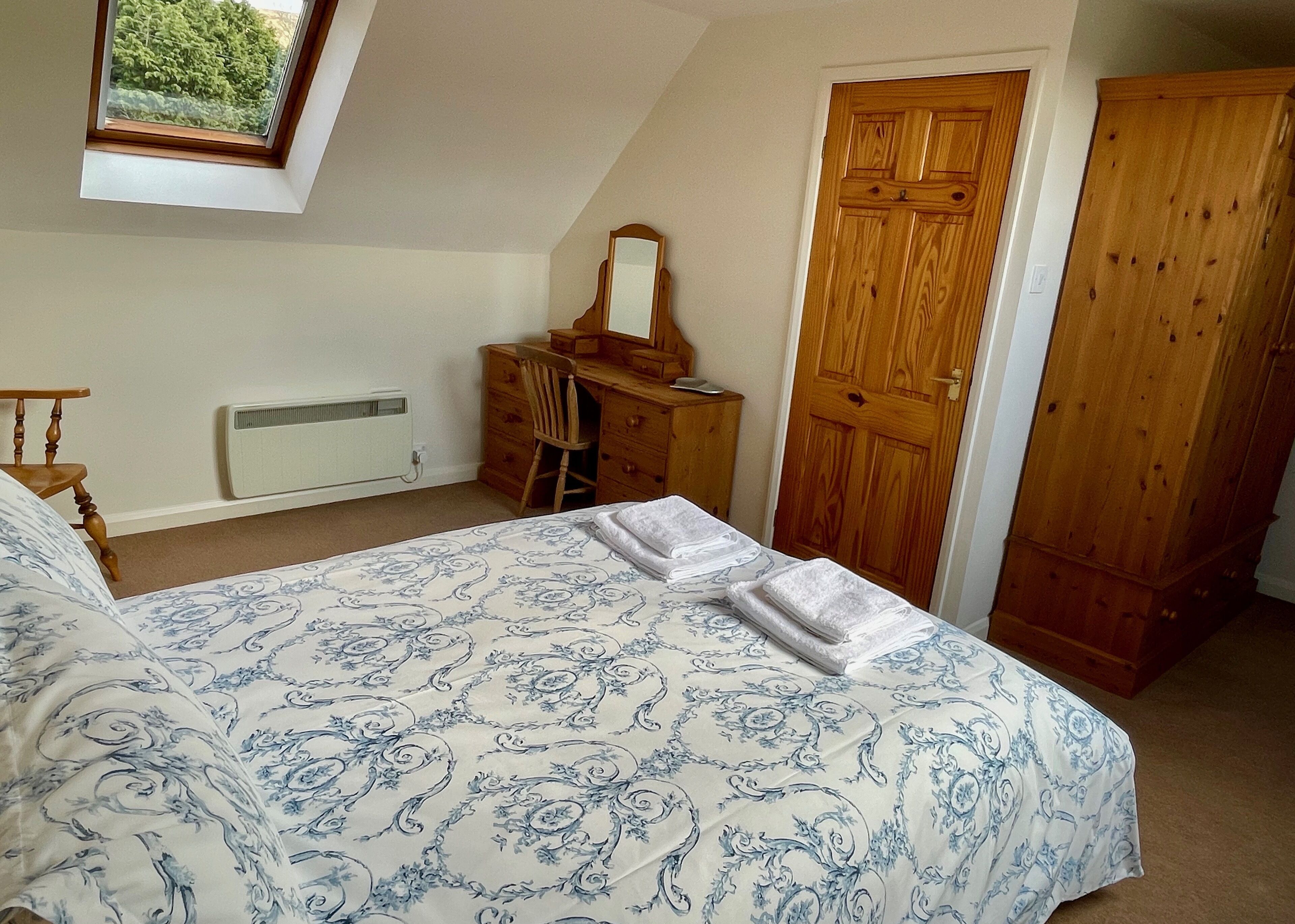 Um quarto com cama, cómoda, cadeira, espelho e guarda-roupa.