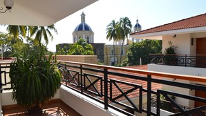 Uma varanda com piso de azulejos, um vaso de planta e vista para um edifício com arquitetura em cúpula.
