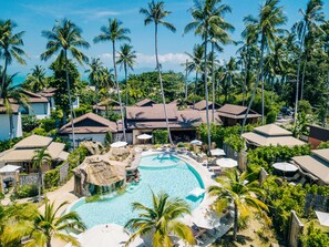 Um resort com piscina, palmeiras e vista para o oceano.