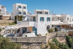 Um edifício branco com persianas azuis, uma parede de pedra e uma piscina.