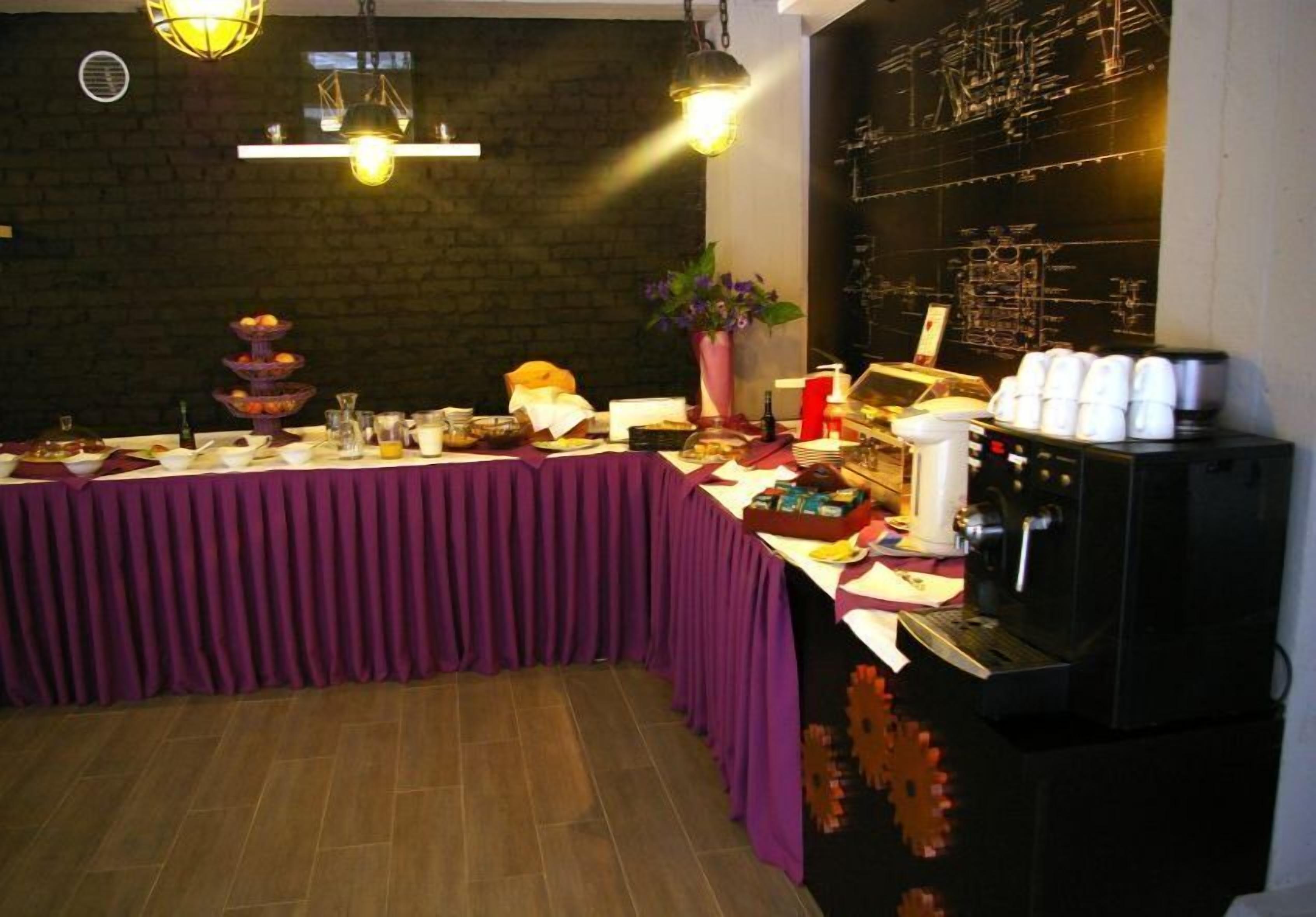 Disposição de buffet com toalha roxa, máquina de café e parede decorativa com instrumentos musicais.