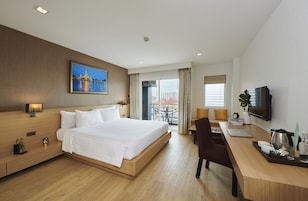 Quarto de hotel com uma cama grande, uma escrivaninha com um laptop, uma televisão e uma varanda com vista para edifícios.