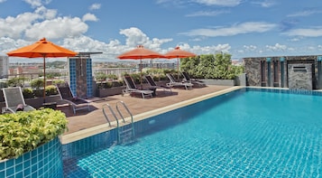 Piscina no terraço com espreguiçadeiras e guarda-sóis laranja, cercada por vegetação e vista da cidade.