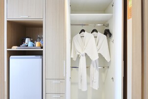 Quarto de hotel com minibar, frigorífico e guarda-roupa com roupões.
