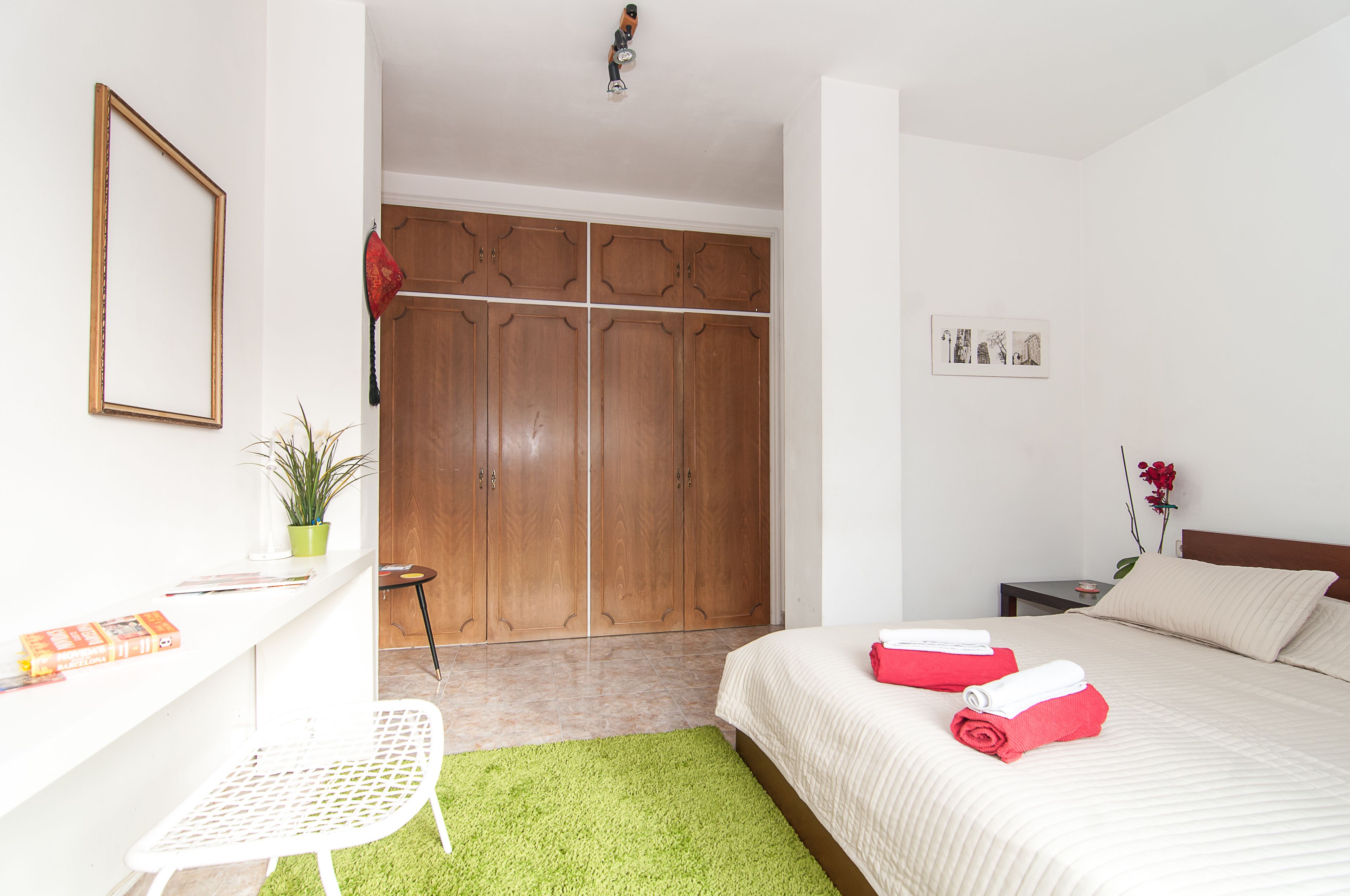 Quarto de hotel com uma cama, uma mesa com cadeira, um guarda-roupa e uma pequena mesa com uma planta.
