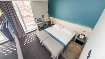 Quarto de hotel com cama, escrivaninha, computador, telefone e janela com cortinas.