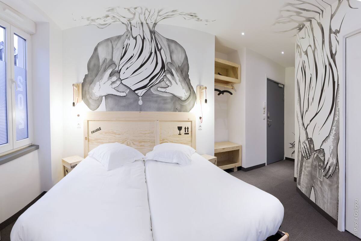 Quarto de hotel moderno com uma cama grande, cabeceira de madeira e um mural na parede.