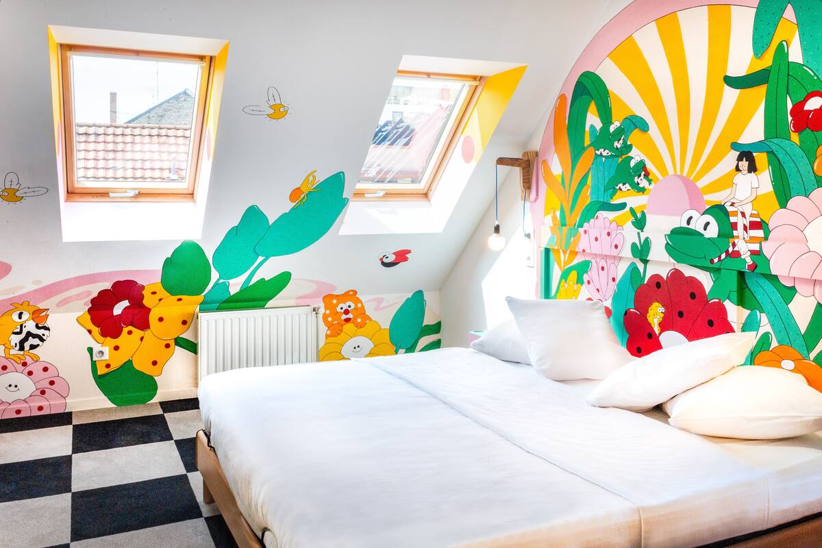 Quarto de criança com cama, duas janelas e decorações coloridas nas paredes.