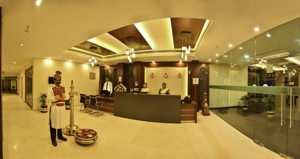 Uma área de recepção de hotel com design moderno, com balcão de atendimento, espaço para sentar e um objeto decorativo central.