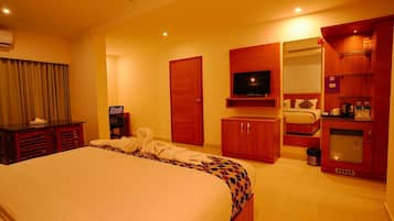 Quarto de hotel com uma cama grande, televisão na parede, guarda-roupa e um pequeno espaço de estar com mesa e cadeiras.