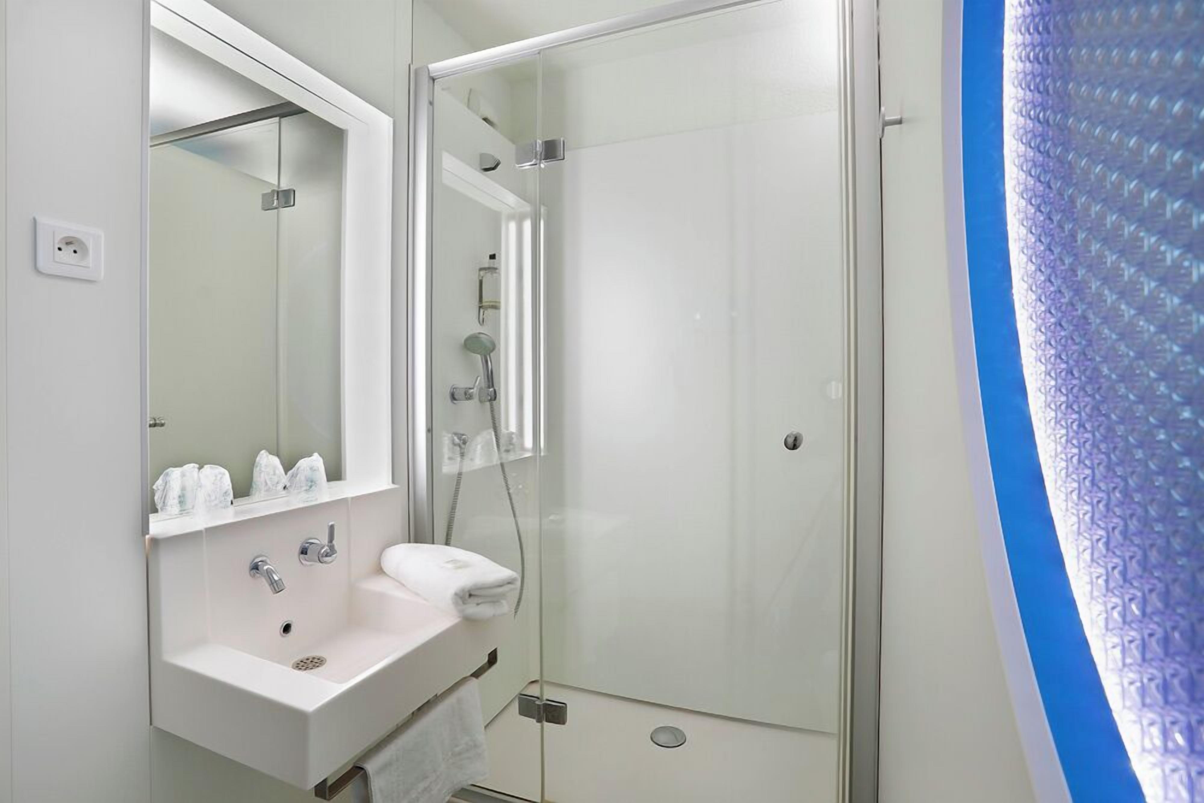 Uma casa de banho moderna com cabine de duche em vidro, lavatório branco com espelho e barra de toalhas.