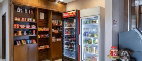 Uma área de distribuição automática com refrigerador de Coca-Cola, freezer e prateleiras repletas de lanches e bebidas.