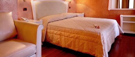 Quarto de hotel com cama, uma cadeira, mesa de cabeceira com abajur e espelho na parede.