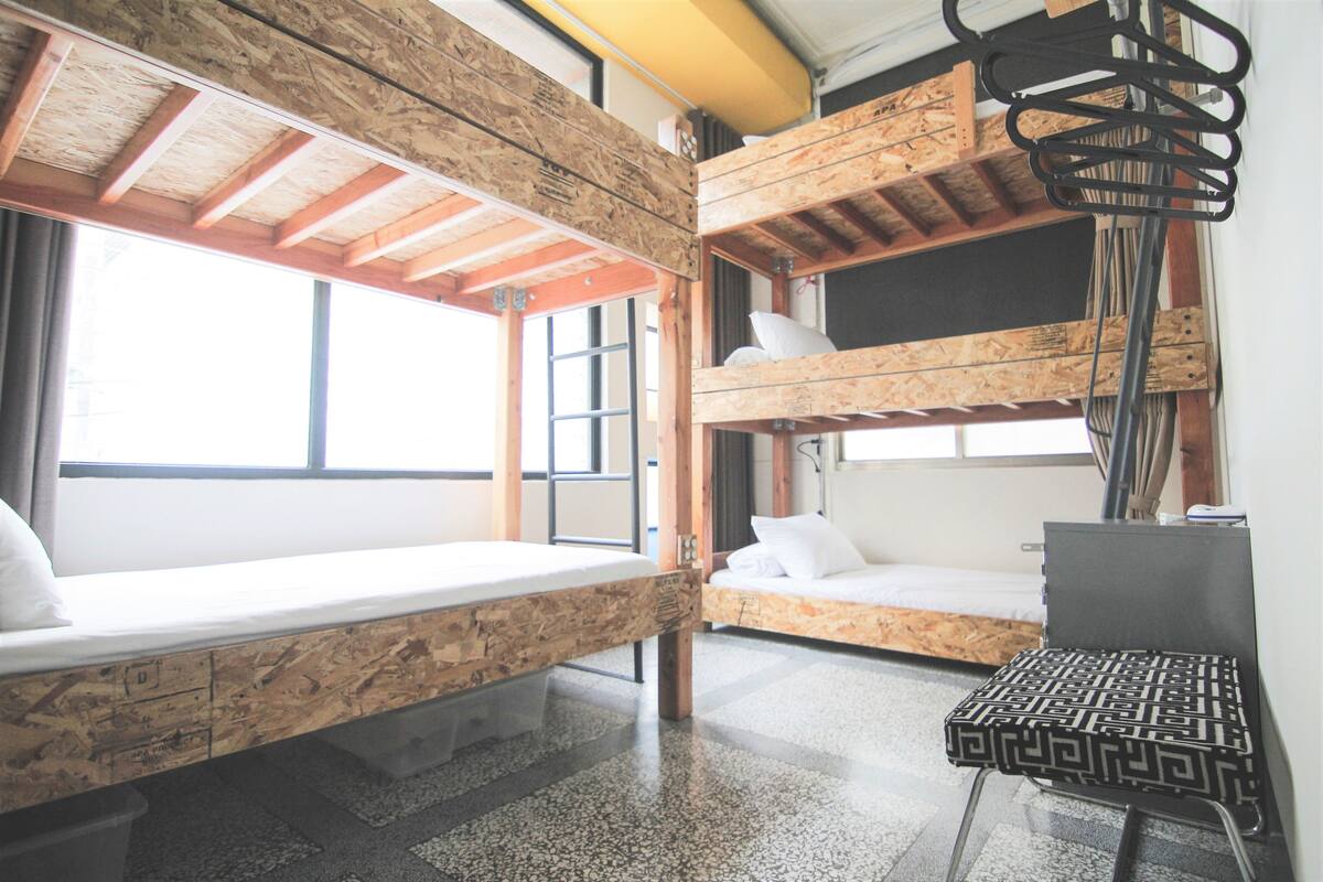 Quarto com beliche, janela, mesa pequena e cadeira suspensa.