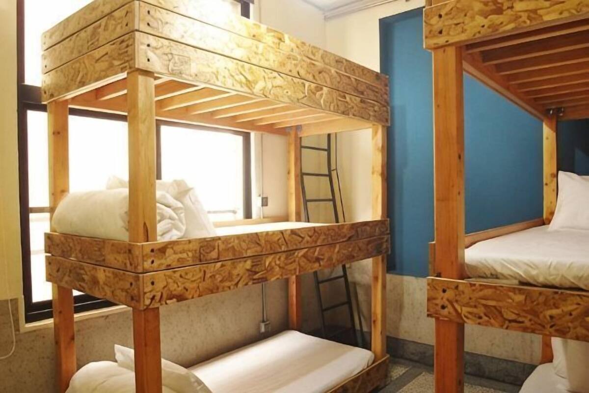 Beliches com estruturas de madeira e roupa de cama branca, uma escada e uma janela.