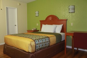 Quarto de hotel com cama, mesa de cabeceira, escrivaninha e porta.