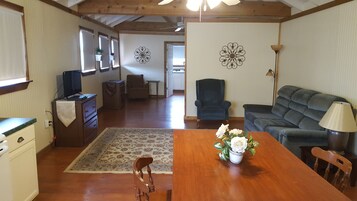 Uma sala de estar acolhedora com uma mesa de madeira, um sofá, uma poltrona e uma TV sobre um aparador.