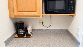 Cozinha com micro-ondas numa prateleira de madeira, máquina de café no balcão e tomada.