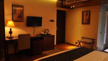 Quarto de hotel com cama, escrivaninha, cadeira, televisão e um pequeno espaço de estar.