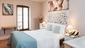Quarto com cama, mesas de cabeceira, escrivaninha e janela.