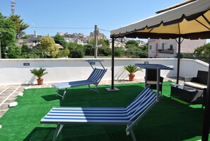 Terraço no telhado com espreguiçadeiras listradas, um espaço de estar coberto e plantas em vasos.