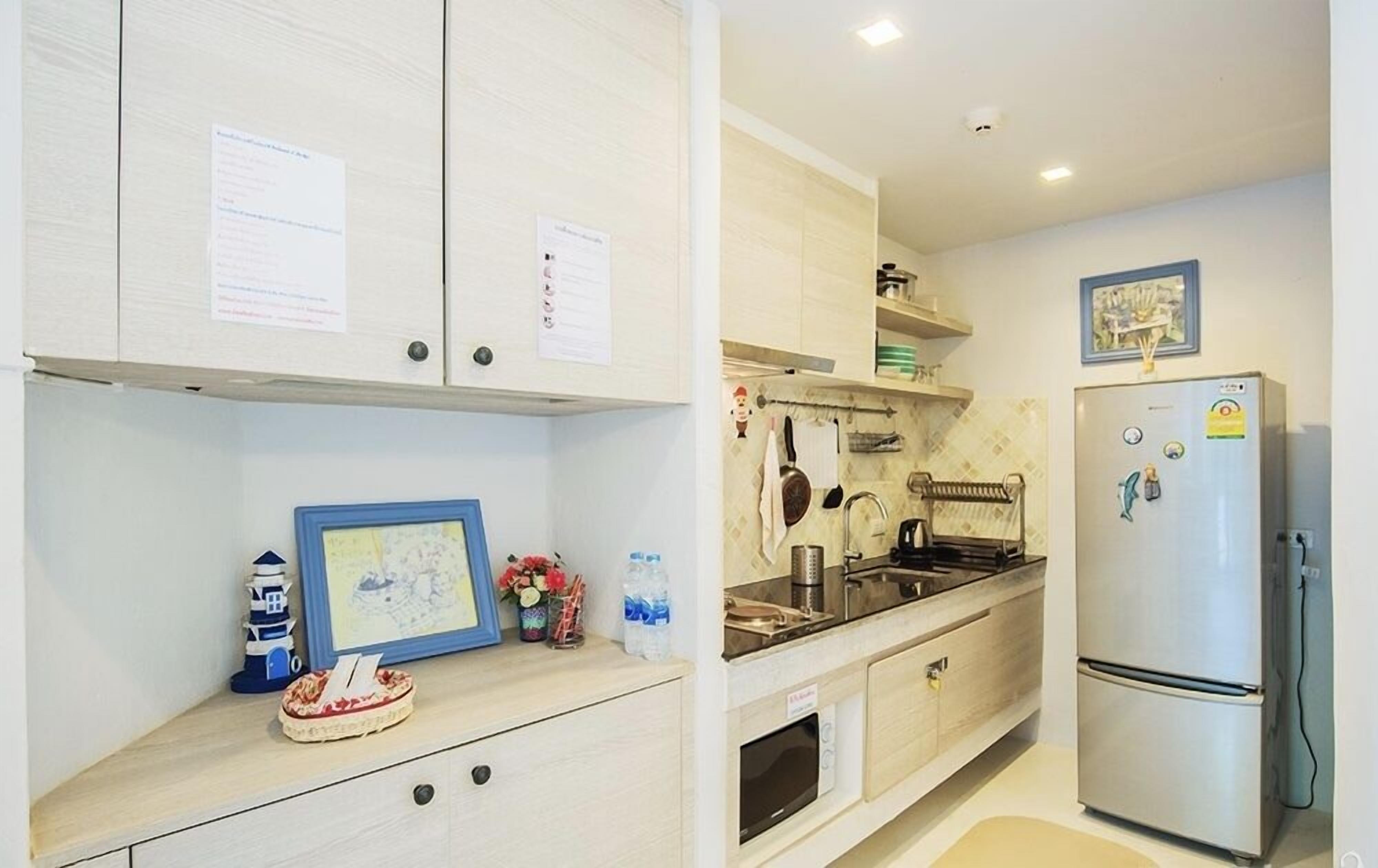 Uma cozinha compacta com micro-ondas, frigorífico e pia. Existem armários acima do balcão e uma pequena prateleira com objetos decorativos.