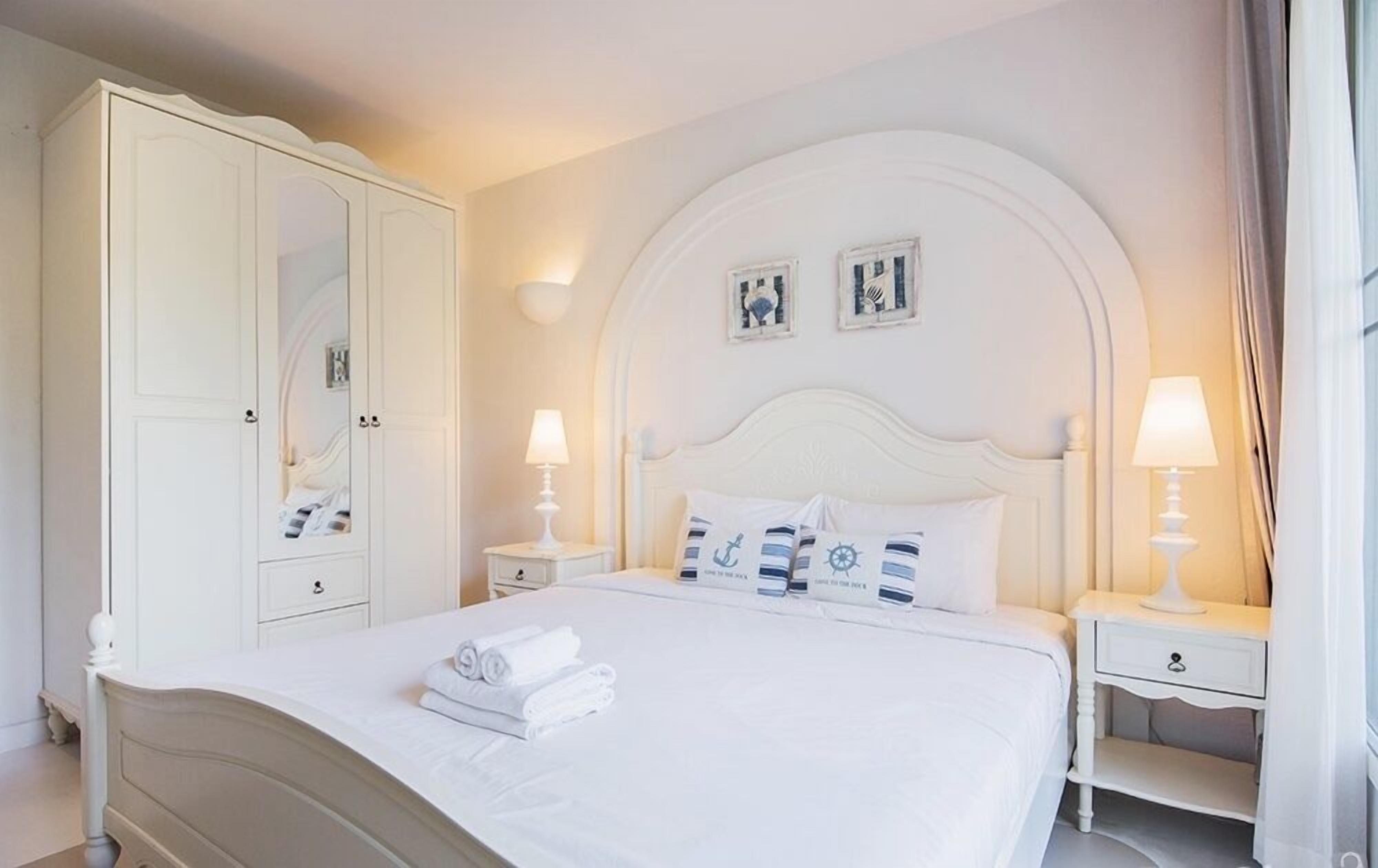 Quarto bem arrumado com uma cama grande, duas mesas de cabeceira, um guarda-roupa e uma parede curva com quadros.
