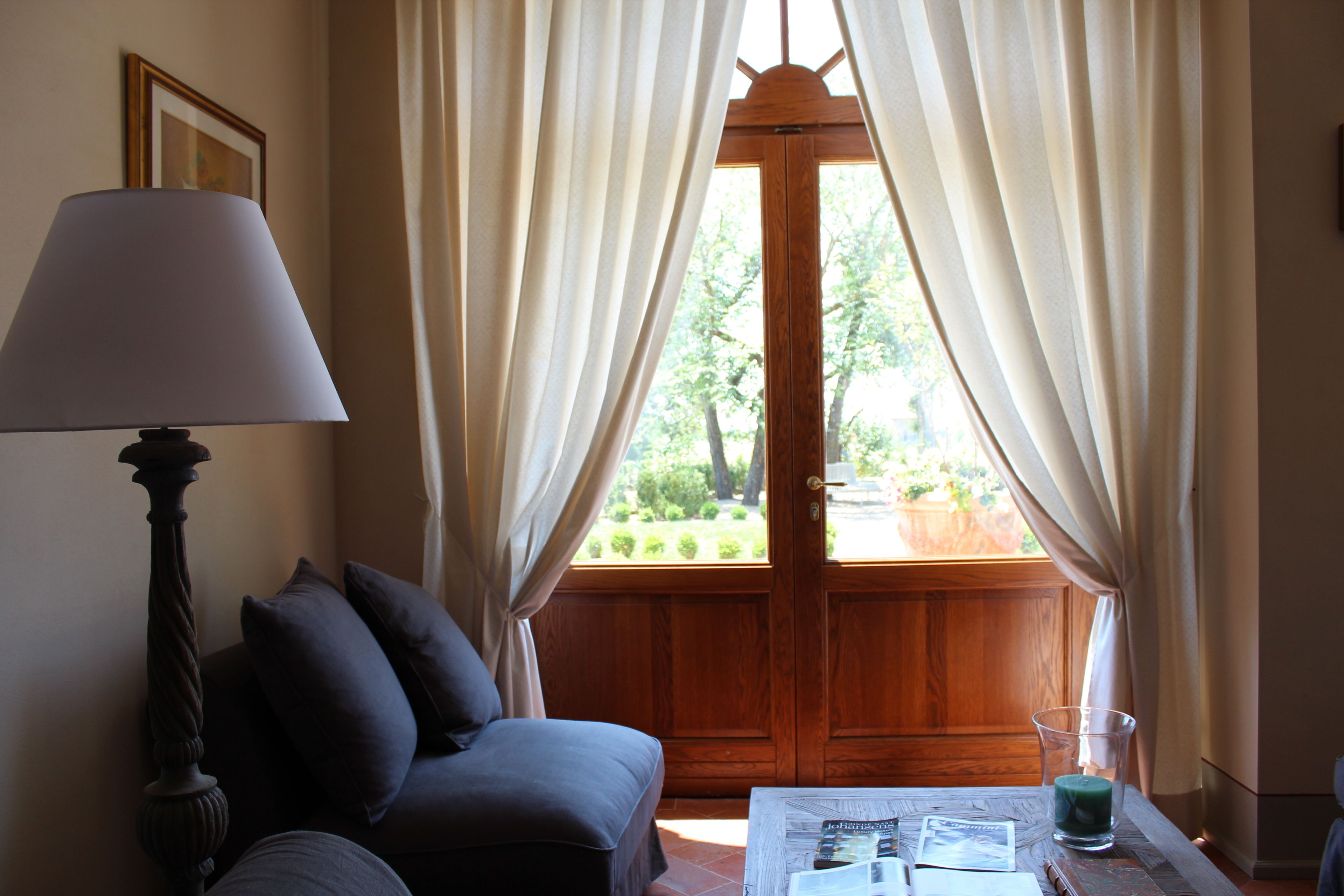 Quarto com porta de madeira, um sofá, uma mesa com um copo de água e um abajur.