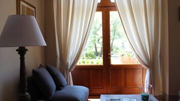 Quarto com porta de madeira, um sofá, uma mesa com um copo de água e um abajur.