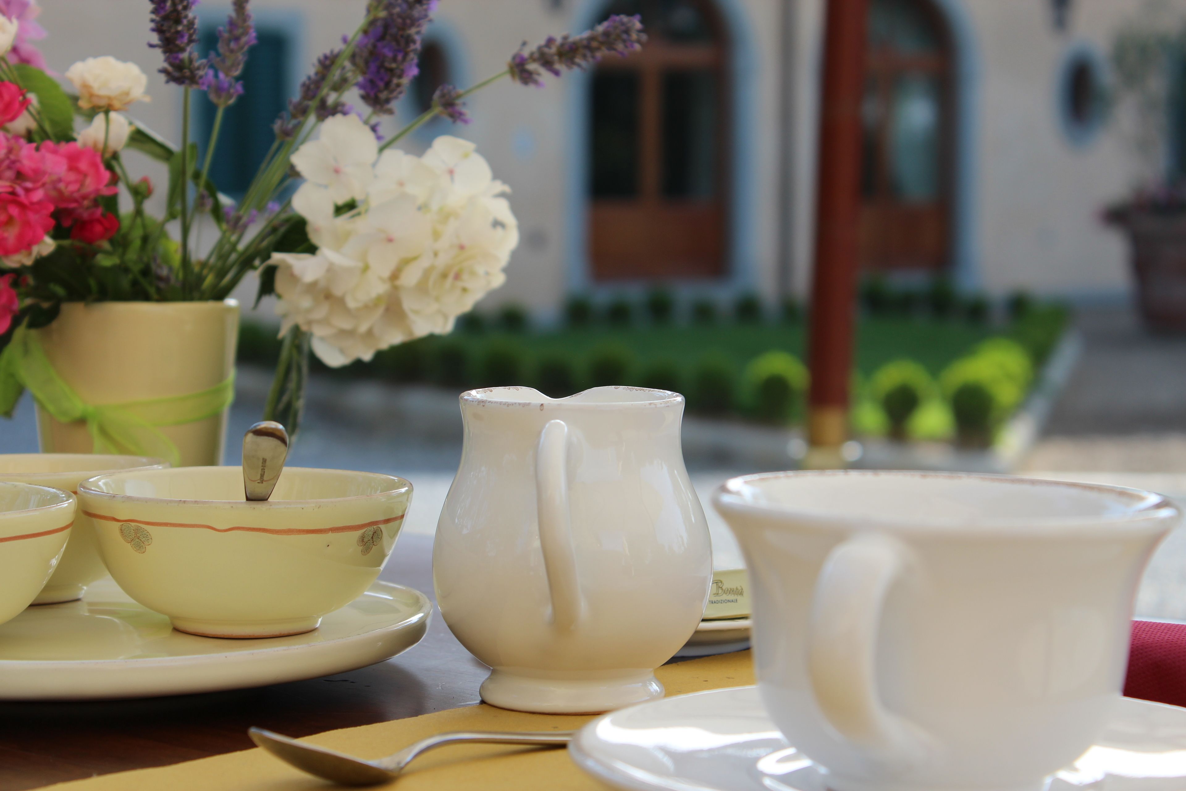 Uma mesa com chávenas e taças de cerâmica branca, um jarro branco e um vaso com flores.