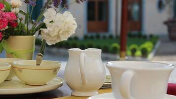 Uma mesa com chávenas e taças de cerâmica branca, um jarro branco e um vaso com flores.