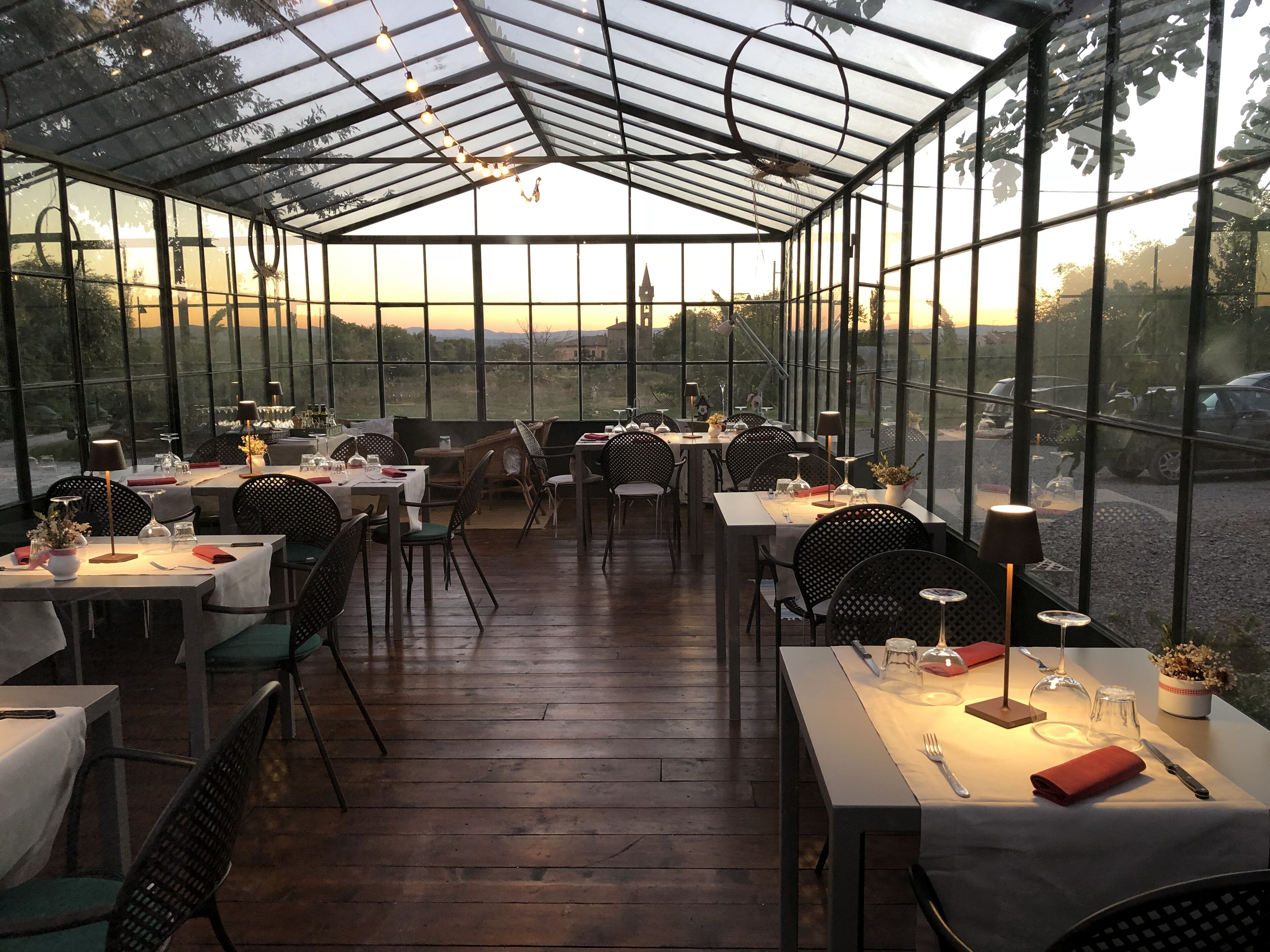 Restaurante com teto de vidro, piso de madeira e mesas preparadas para refeições.