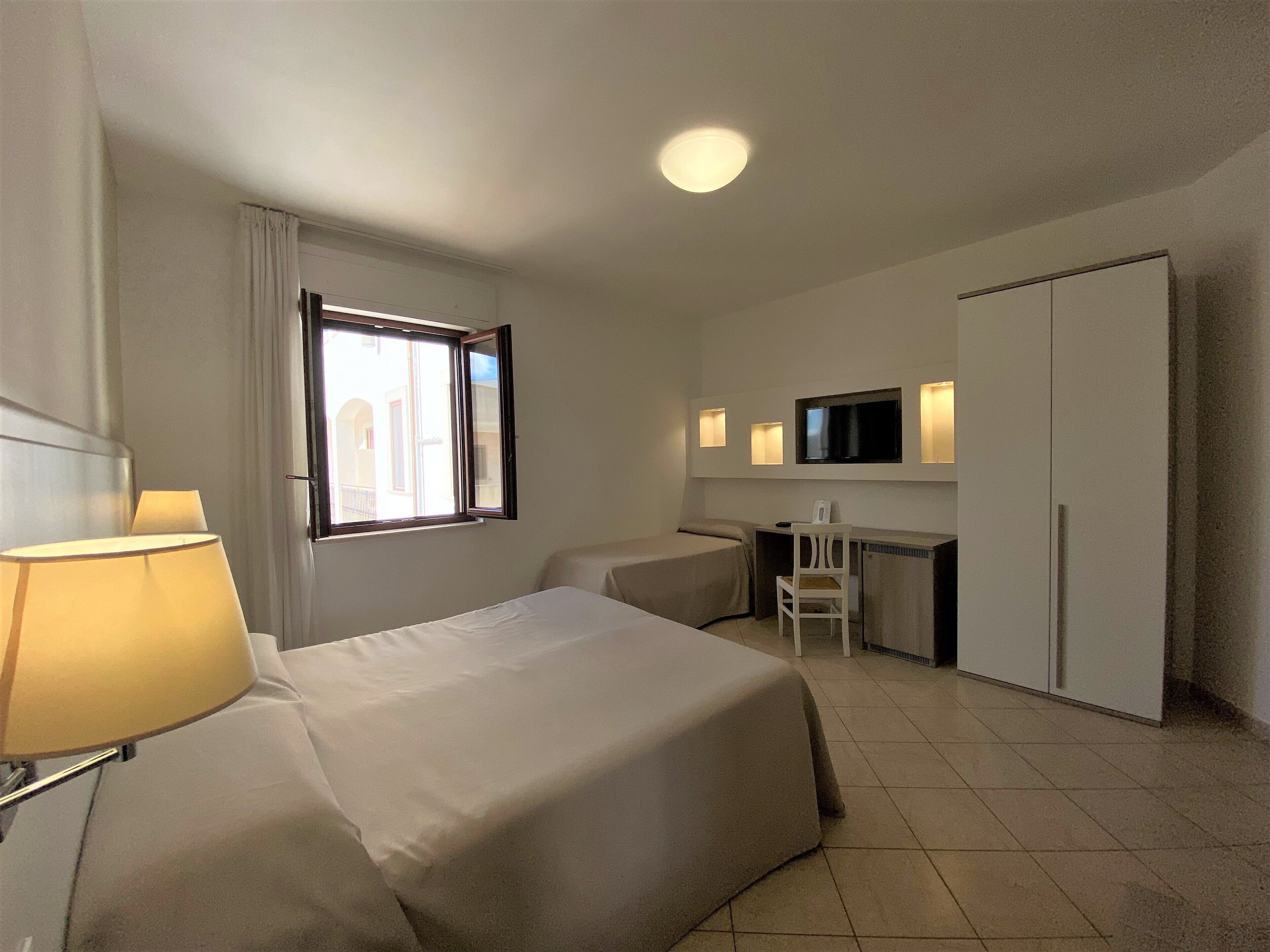 Quarto de hotel com cama, escrivaninha, cadeira, televisão e armário.