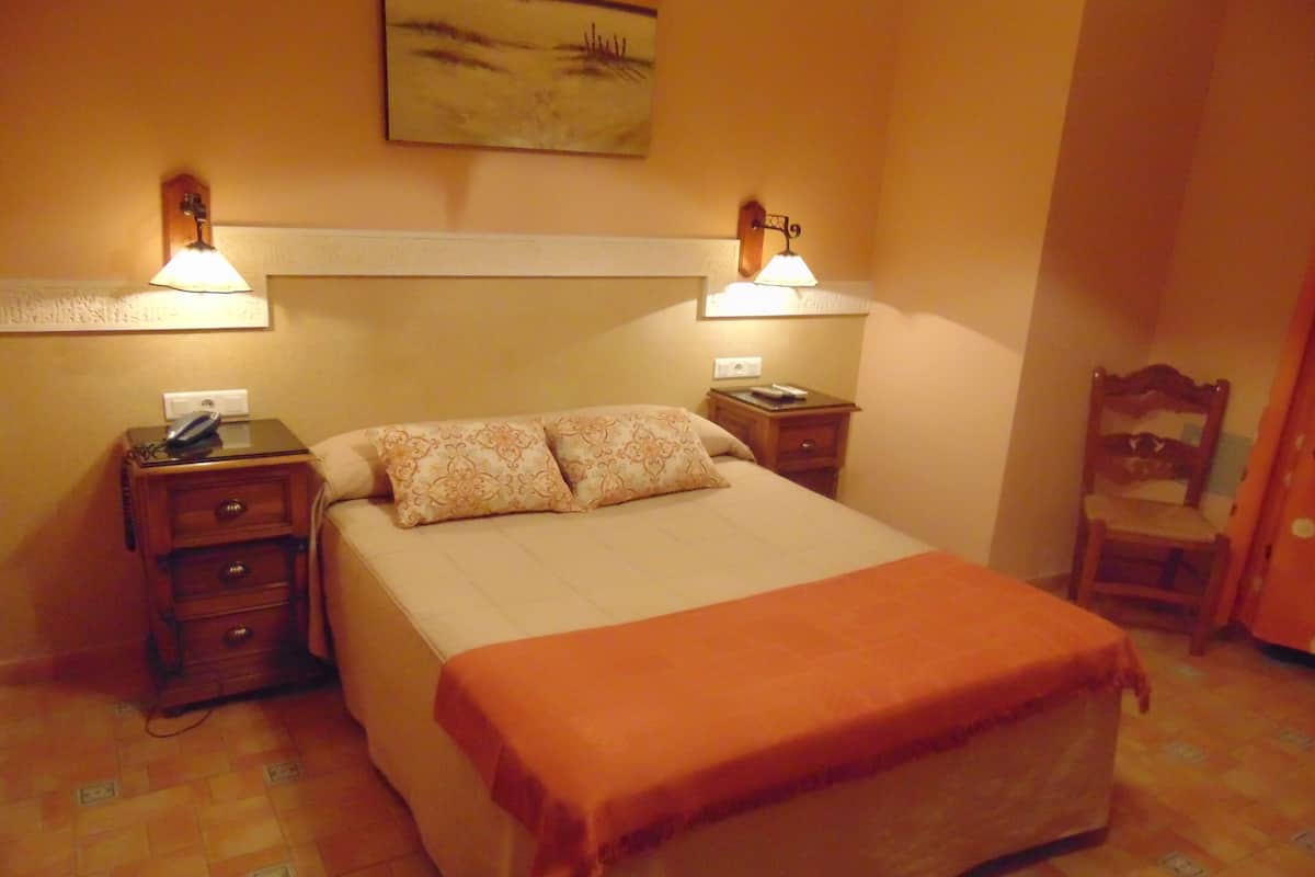 Uma cama bem arrumada com cabeceira, duas mesas de cabeceira com luminárias, uma cadeira e um quadro na parede.