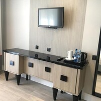 Quarto de hotel moderno com bancada preta, armários de madeira e televisão na parede.