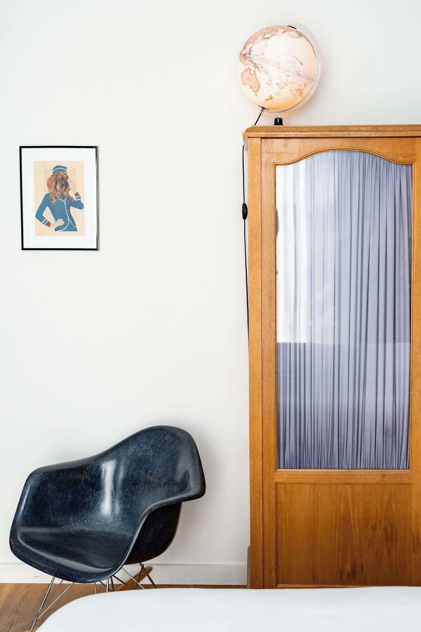 Quarto com porta de madeira, um globo em cima, um quadro emoldurado e uma cadeira preta.
