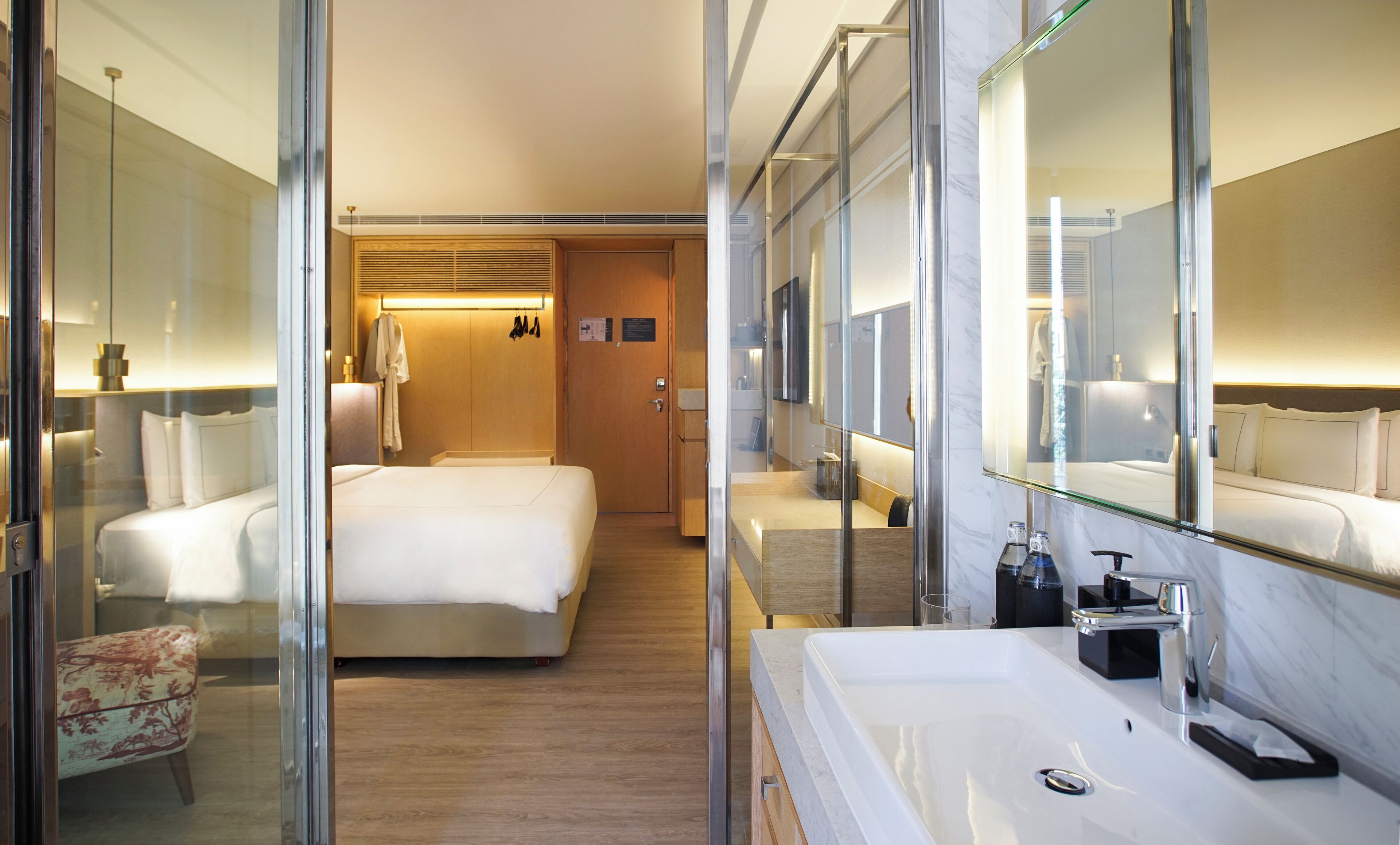 Quarto de hotel com uma cama grande, banheiro separado com espelho e uma pequena área de estar.
