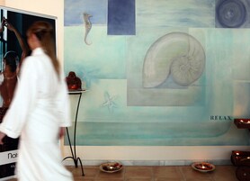 Quarto com um grande mural abstrato, uma pequena mesa com uma estátua de Buda e duas tigelas com velas no chão.
