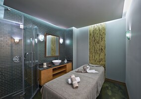 Casa de banho moderna com chuveiro envidraçado, toucador com lavatório e espelho, e cama com toalhas.