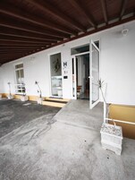 Entrada de hotel com piso de concreto, teto de madeira e parede externa branca.