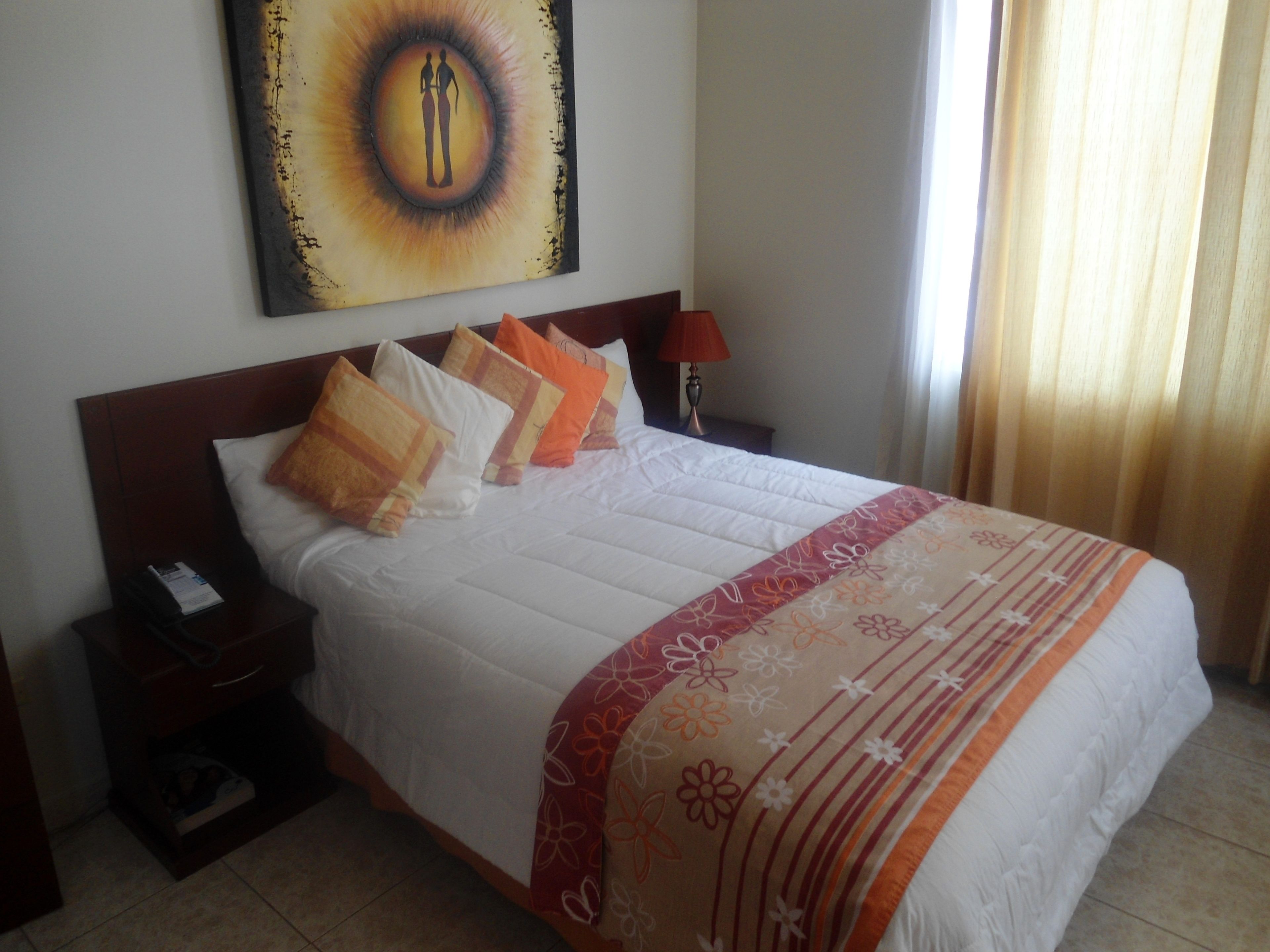 Quarto de hotel com cama, mesa de cabeceira, abajur e um quadro na parede.